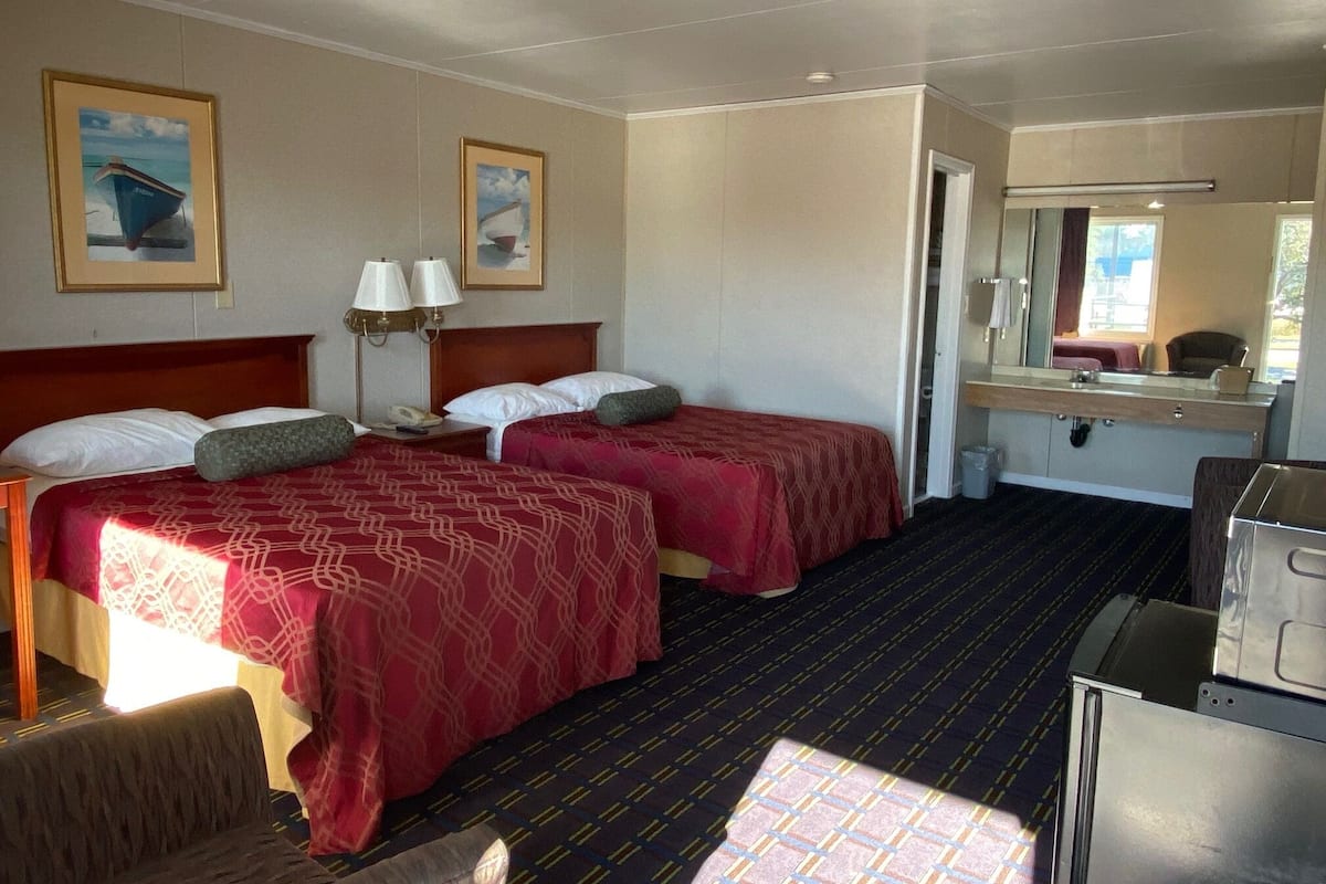 Quarto de hotel com duas camas, uma escrivaninha, um espelho e uma janela.