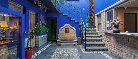 Um corredor com paredes azuis, soalho em mosaicos, uma escadaria e uma porta que dá para um quarto.