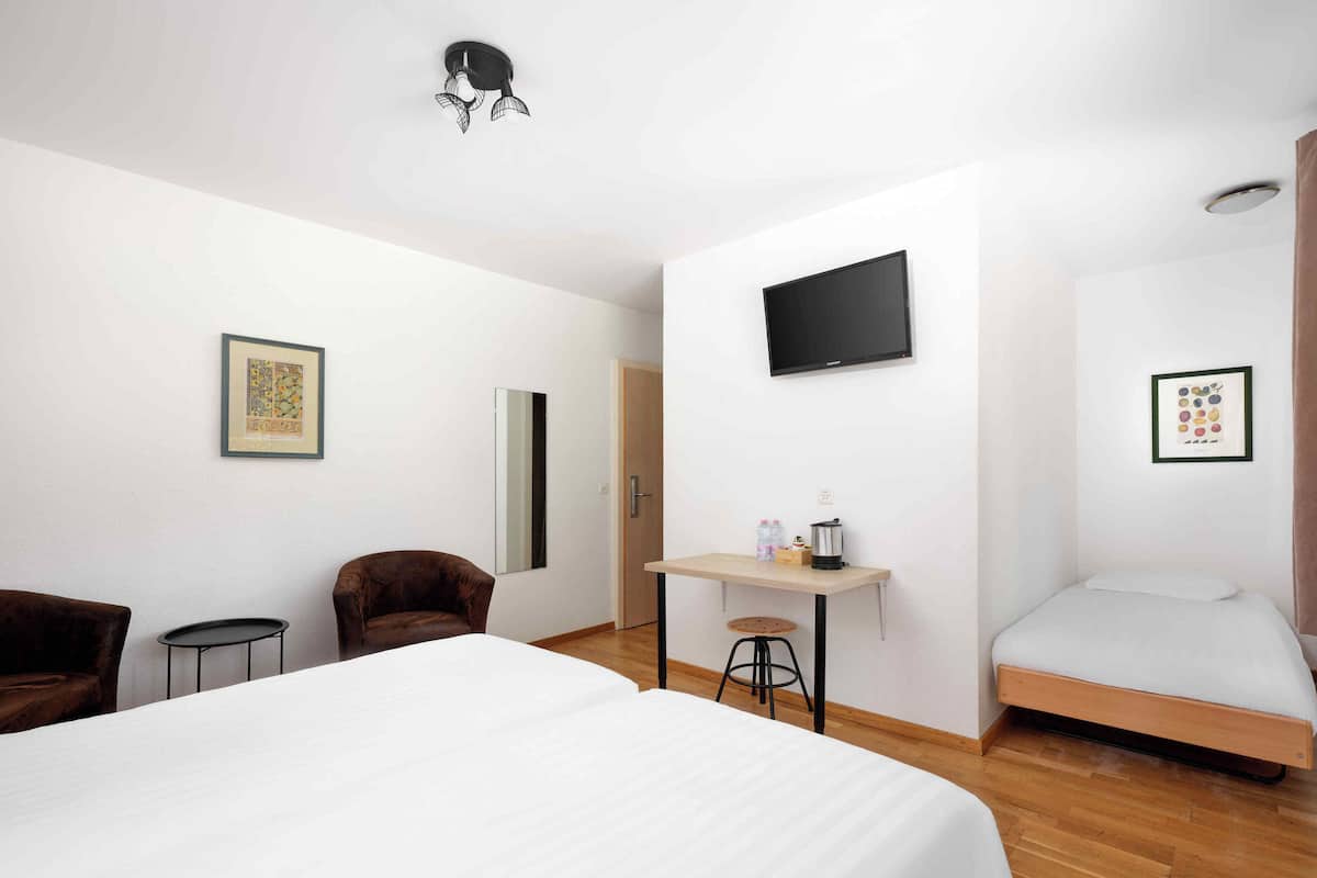 Quarto de hotel com uma cama, uma escrivaninha com cadeira, televisão e duas fotos emolduradas na parede.