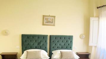 Quarto com duas camas, um lustre, um quadro emoldurado na parede e uma janela com cortinas.