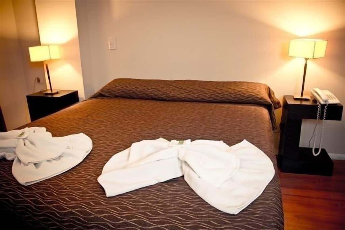 Uma cama bem arrumada com um edredom marrom estampado e duas toalhas brancas sobre ela.