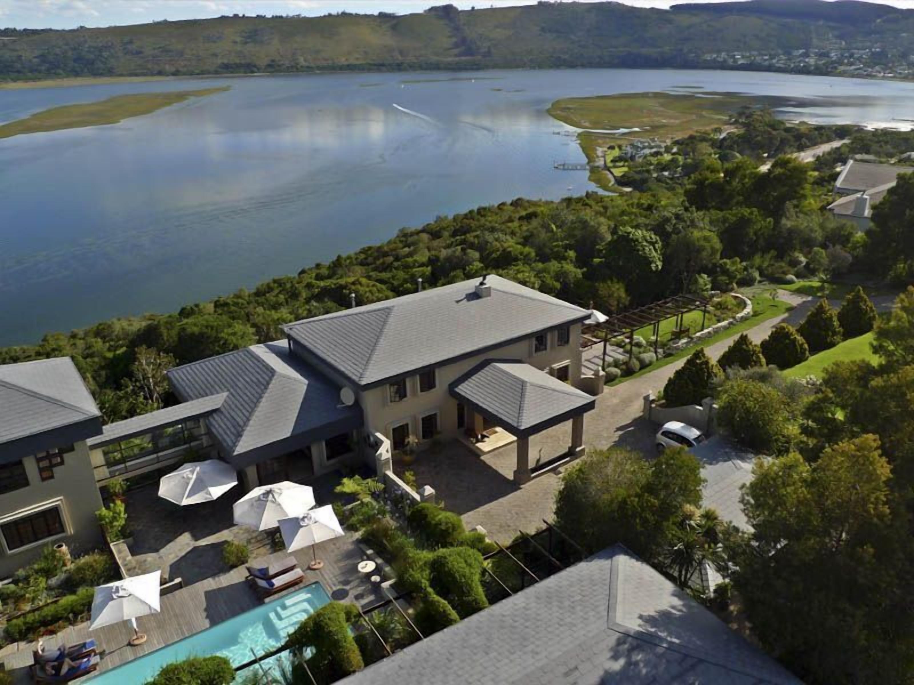 Uma casa grande com piscina, rodeada por vegetação exuberante e um lago.