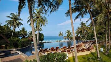 Uma área de piscina em resort, com espreguiçadeiras, palmeiras e vista para o oceano.