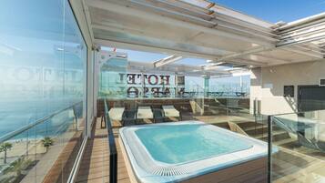 Um terraço no telhado com hidromassagem, guarda-corpos de vidro e vista para o oceano.