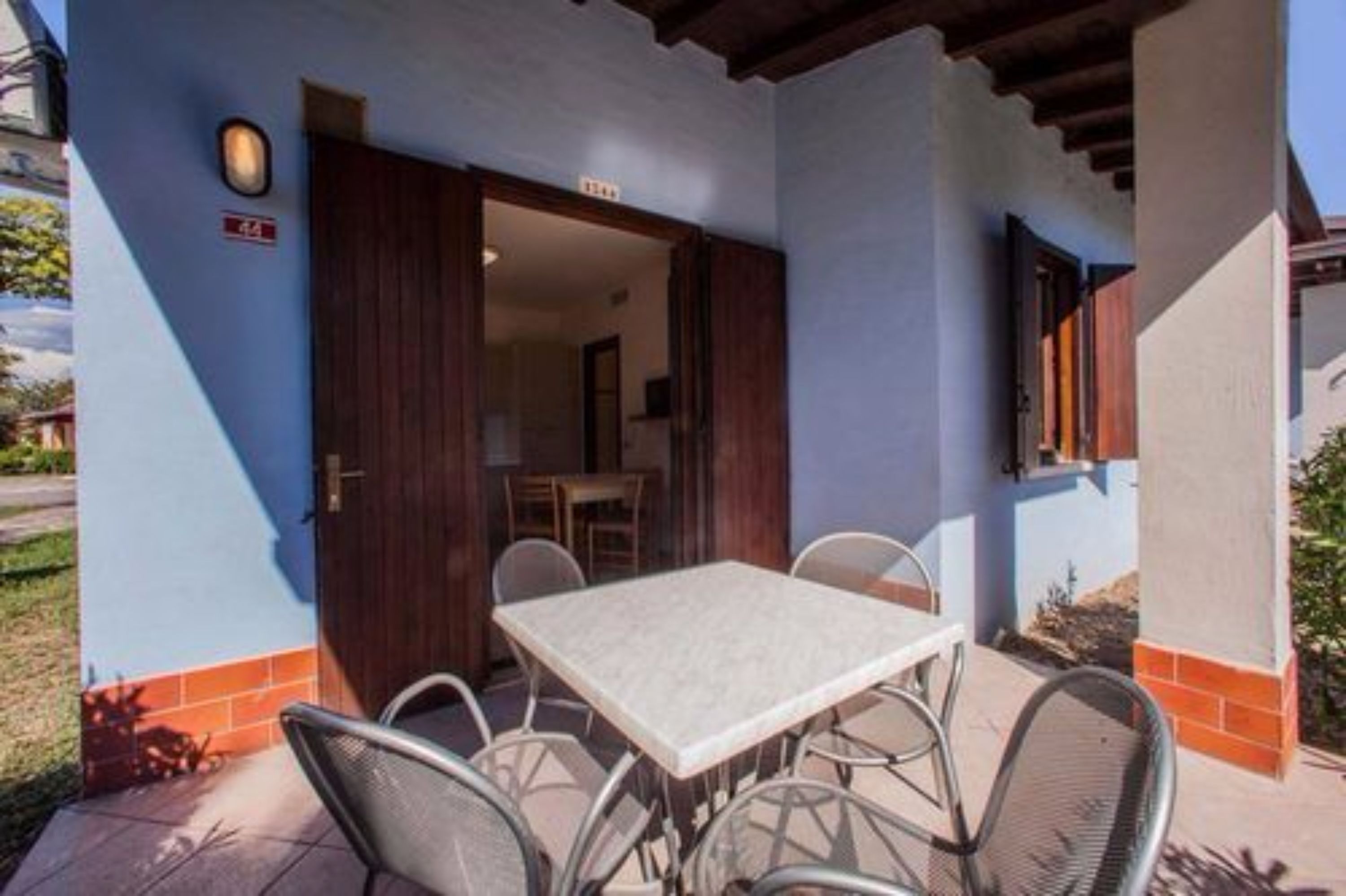 Um pátio externo com mesa e cadeiras, uma porta de madeira e uma janela com persianas de madeira.