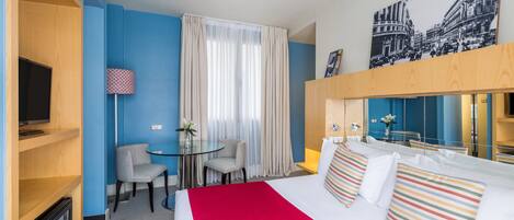 Quarto de hotel com cama, televisão, escrivaninha com cadeira e janela com cortinas.