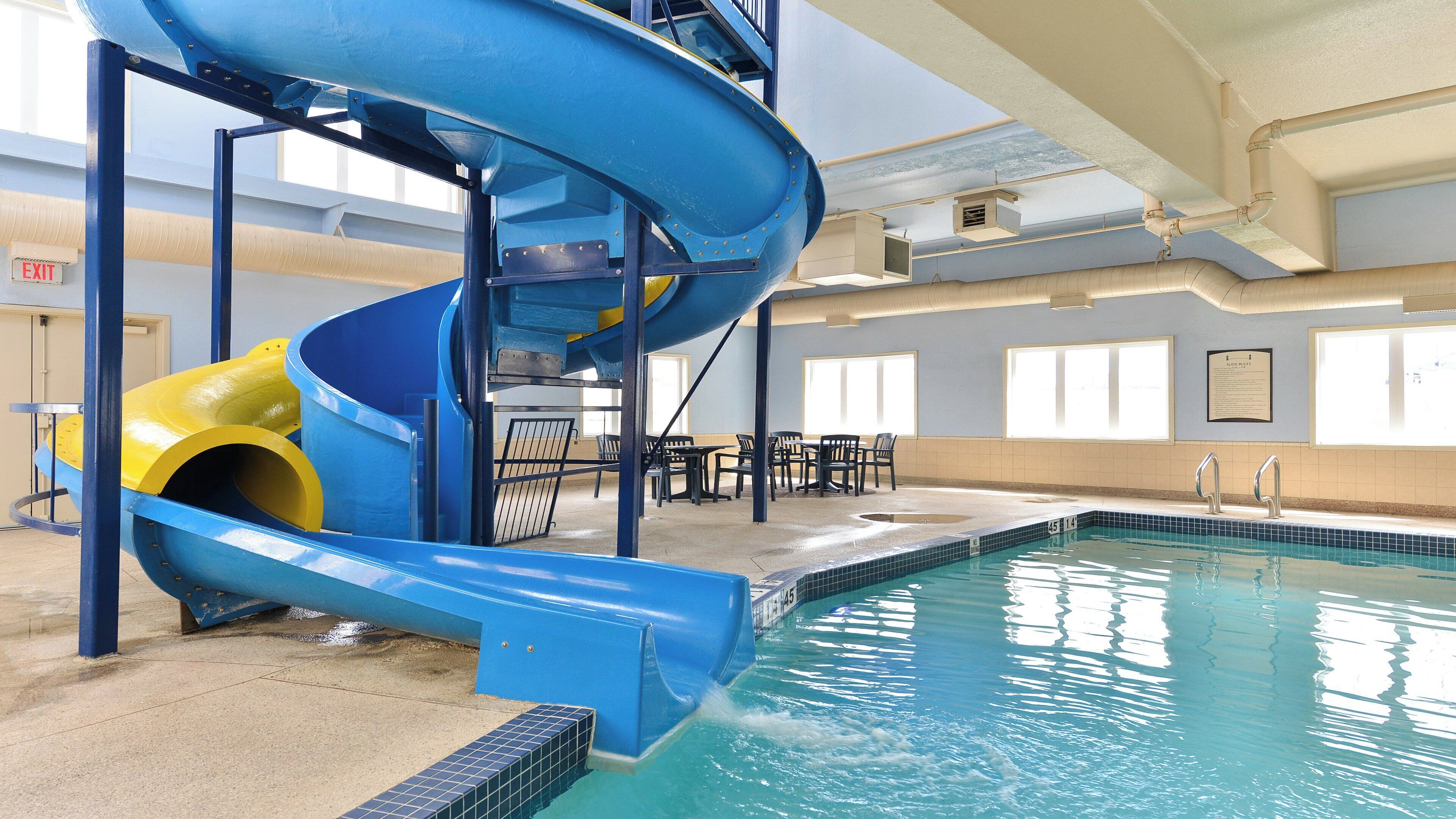 Piscina interna com tobogã azul e amarelo, área de estar e vista clara da borda da piscina.