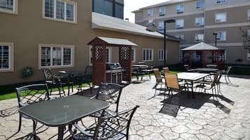 Uma área de pátio externa com mesas e cadeiras, churrasqueira e um gazebo.