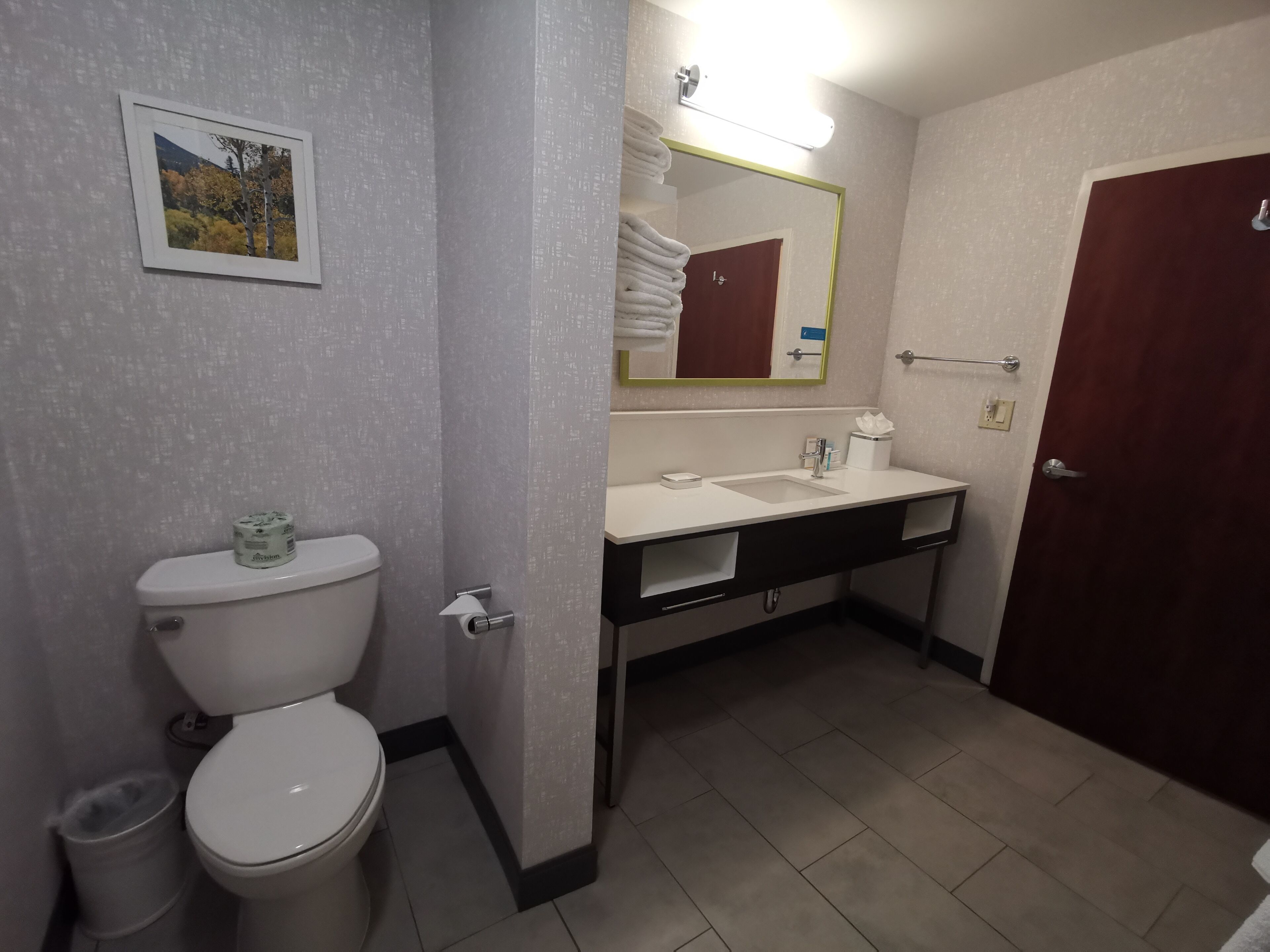 Casa de banho com sanita, lavatório, espelho e porta.