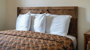 Uma cama com cabeceira de madeira, almofadas brancas e colcha estampada.