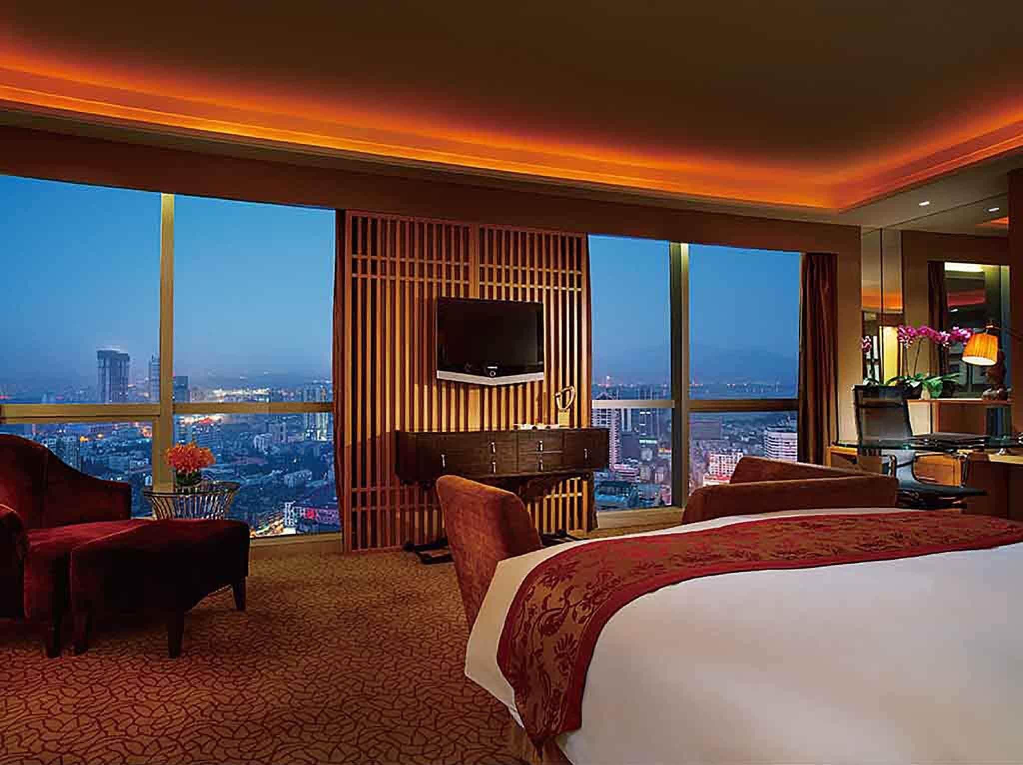 Quarto de hotel com uma cama grande, televisão, escrivaninha e vista para a paisagem urbana.