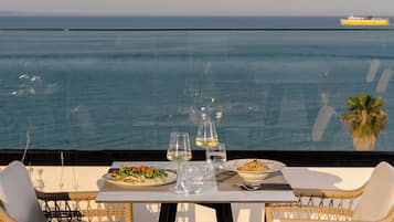 Uma mesa de jantar com pratos de comida, copos e vista para o oceano.