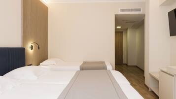 Quarto de hotel com duas camas, uma mesinha de cabeceira, uma luminária, uma televisão e parede de painel de madeira.