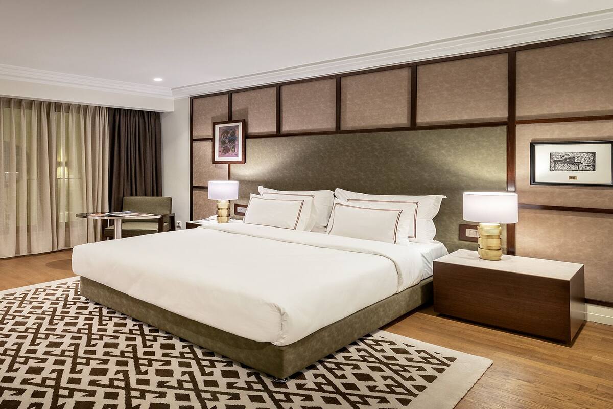 Quarto de hotel com cama grande, mesas de cabeceira com luminárias, escrivaninha e uma cadeira.