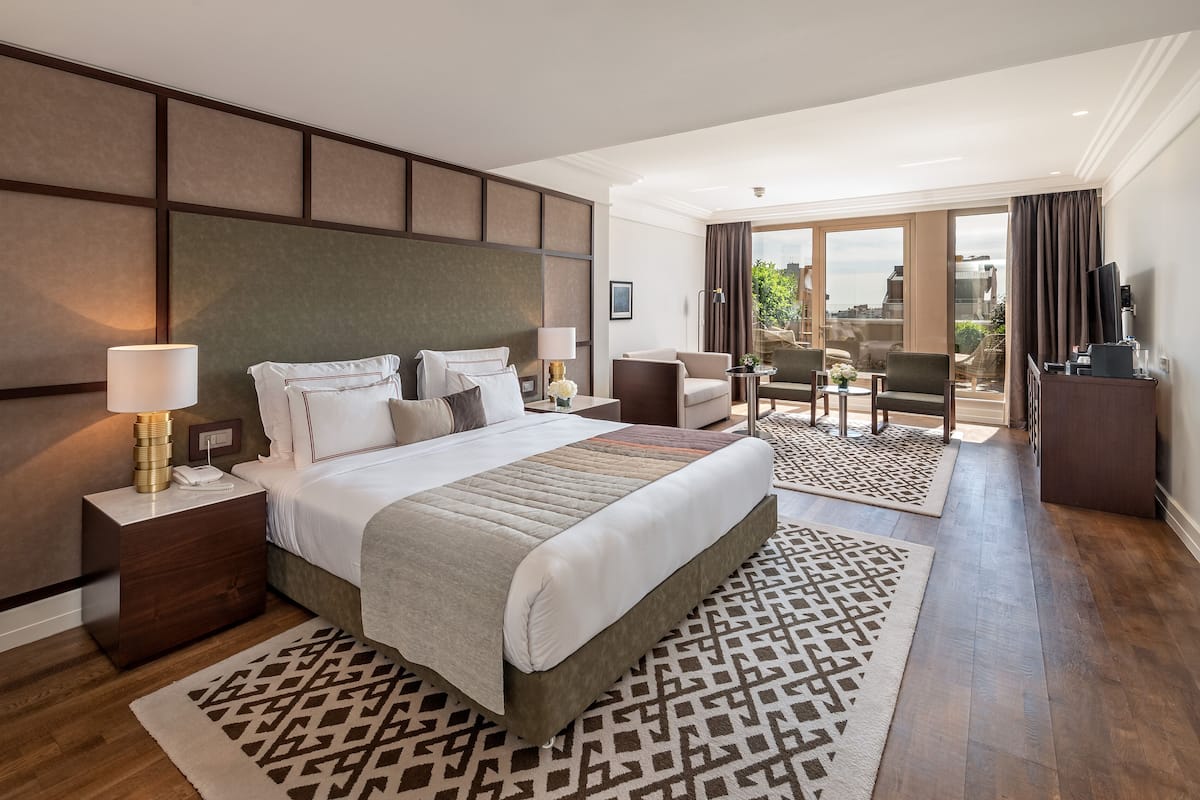 Quarto de hotel moderno com uma cama grande, uma escrivaninha, uma cadeira e uma varanda com vista.