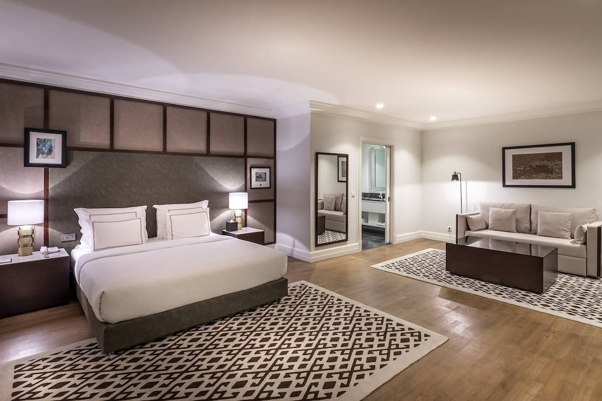 Quarto de hotel moderno com uma cama grande, um sofá, uma escrivaninha e um espelho.