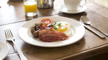 Prato de café da manhã com ovos, bacon, cogumelos e tomates sobre uma mesa de madeira.