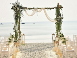 Decoração de casamento na praia, com um corredor branco, flores e lanternas.