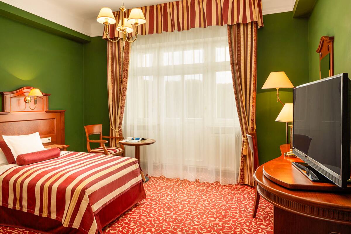 Quarto de hotel com cama, televisão, escrivaninha e cadeira.