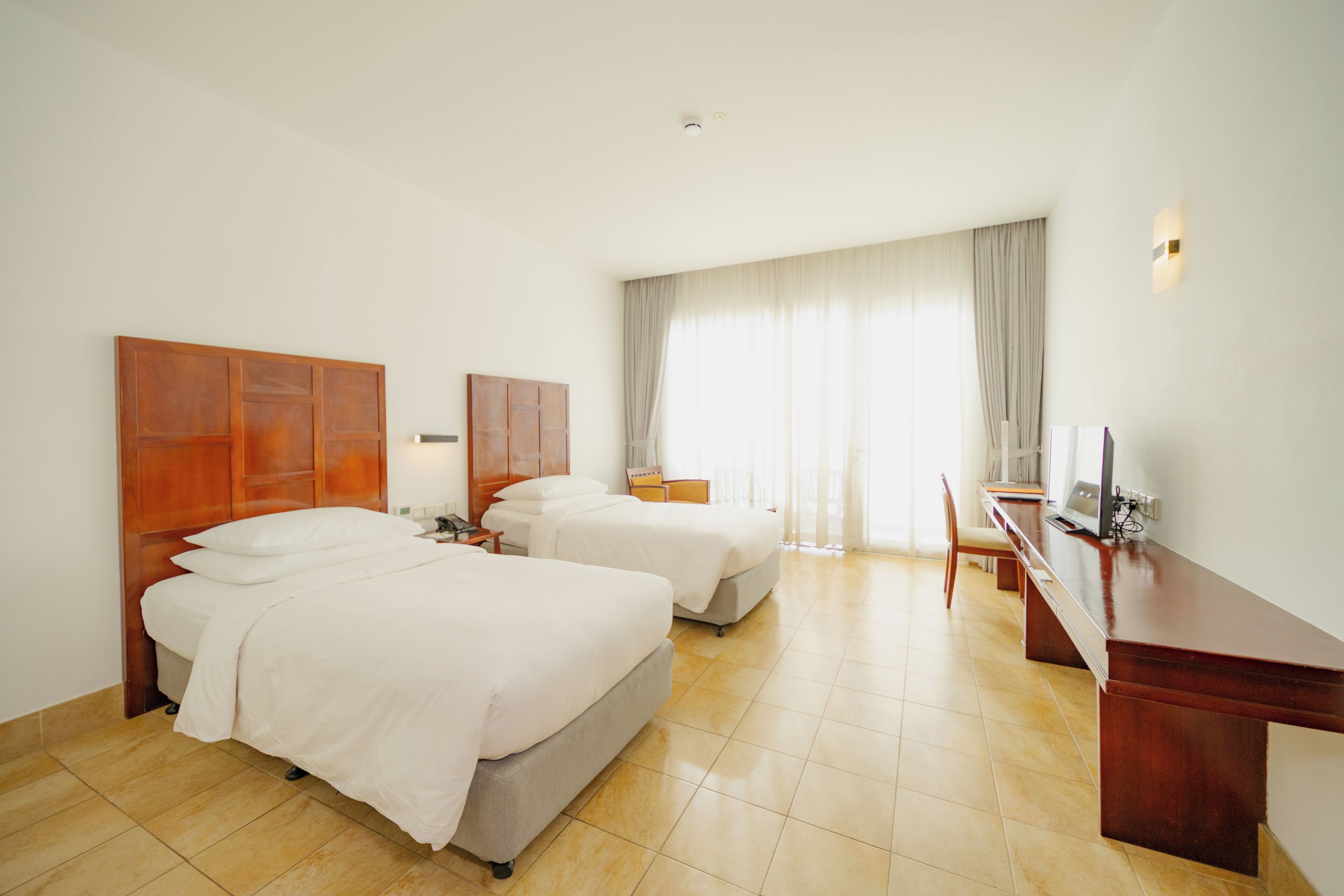 Quarto de hotel com duas camas, uma escrivaninha, uma cadeira e uma televisão.