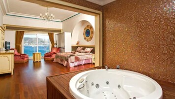Quarto espaçoso com uma cama grande, um espaço de estar com uma poltrona, uma banheira grande e vista para o mar através de uma janela ampla.