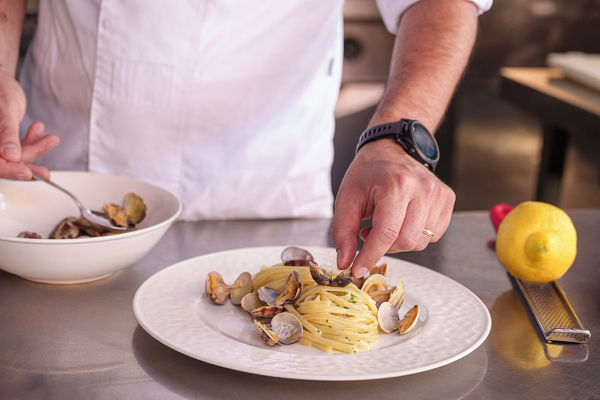 Um chef preparando um prato com massa e amêijoas em um prato branco.