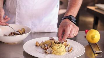 Um chef preparando um prato com massa e amêijoas em um prato branco.
