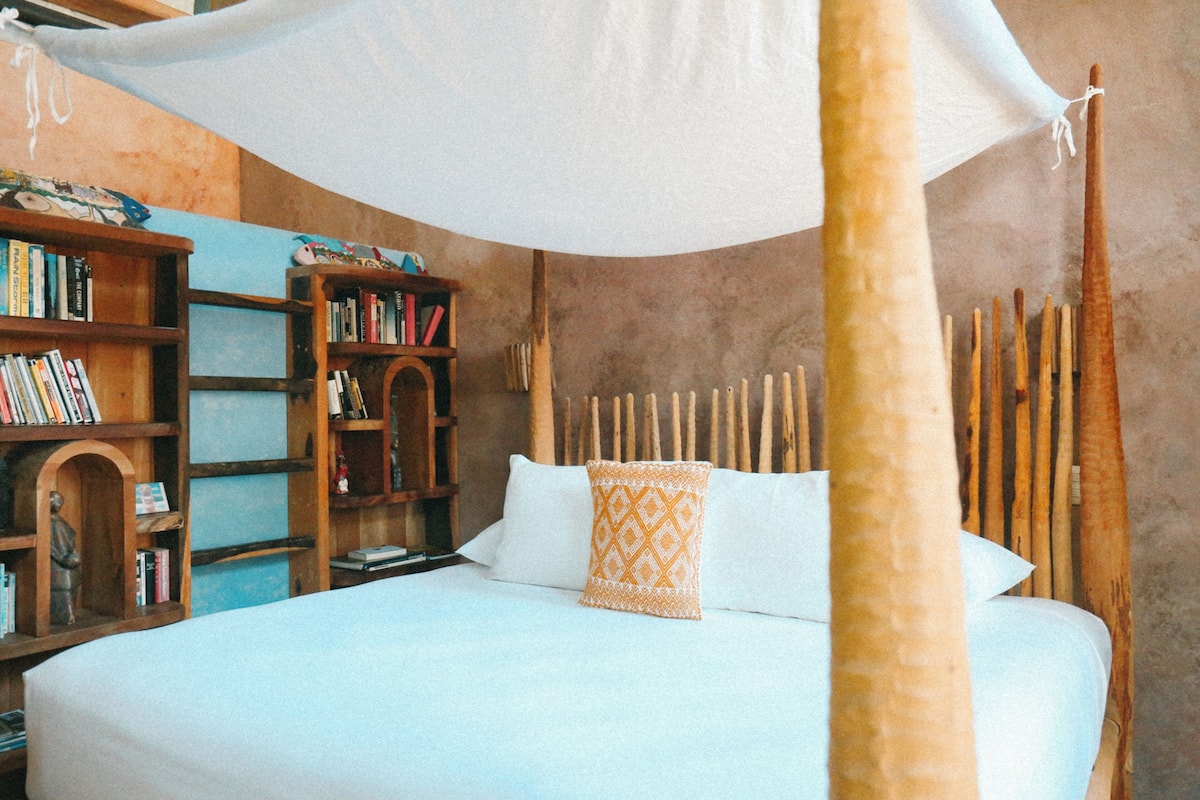 Quarto com cama de dossel, estantes de madeira e parede rústica.