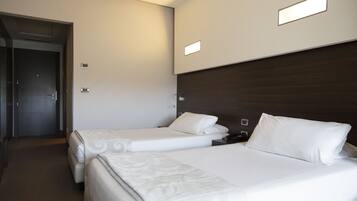 Quarto de hotel com duas camas, cabeceira em madeira escura, piso coberto por carpete e porta que dá para outro cômodo.