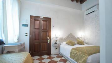 Quarto com chão xadrez, cama com colcha estampada, mesa de cabeceira com luminária e porta com fechadura.