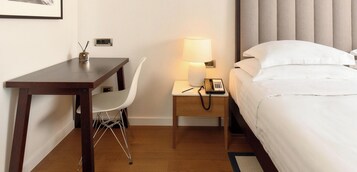Quarto de hotel com uma cama, escrivaninha, cadeira, abajur e telefone.