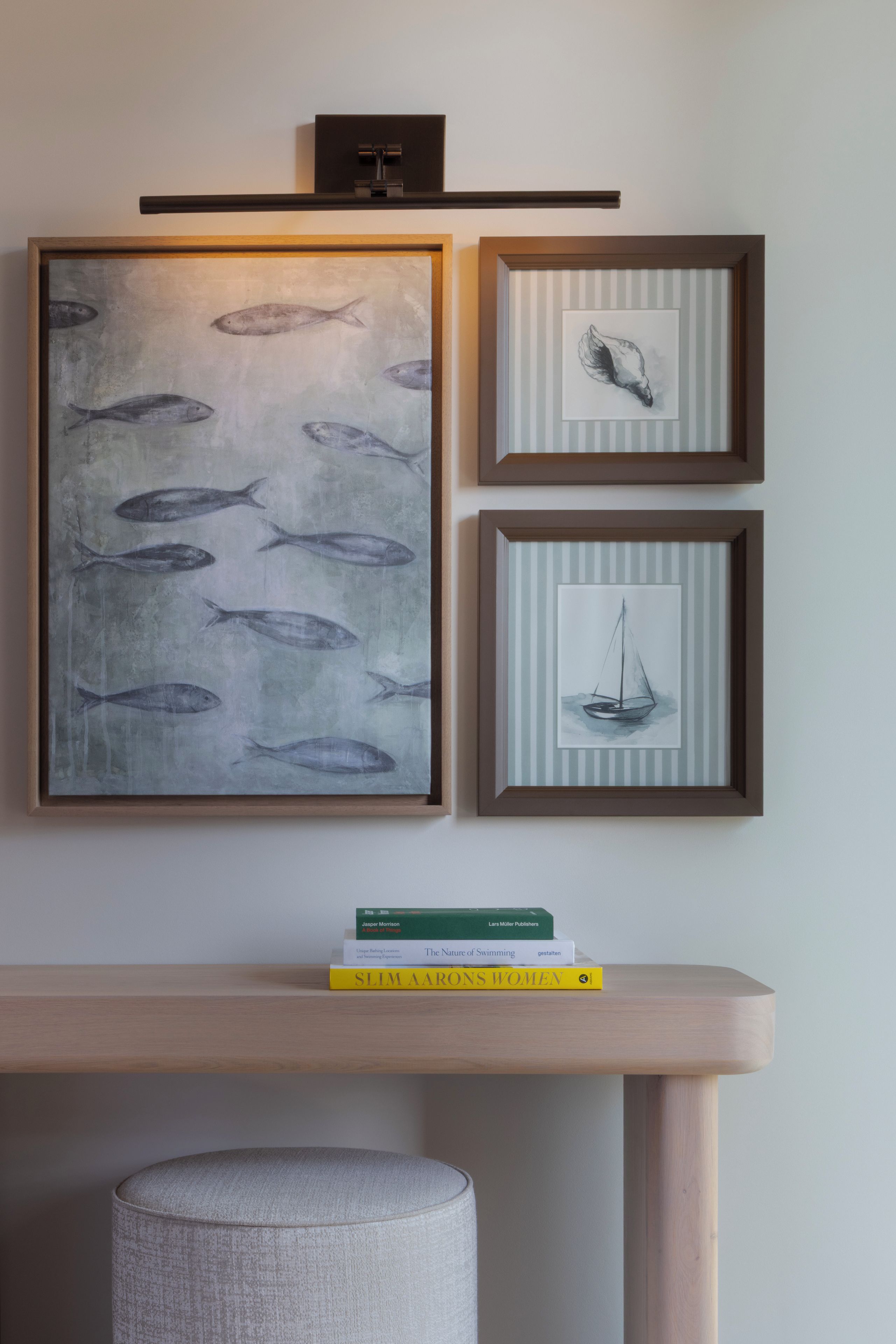 Paredes decoradas com três quadros, uma pilha de livros e um banquinho redondo.