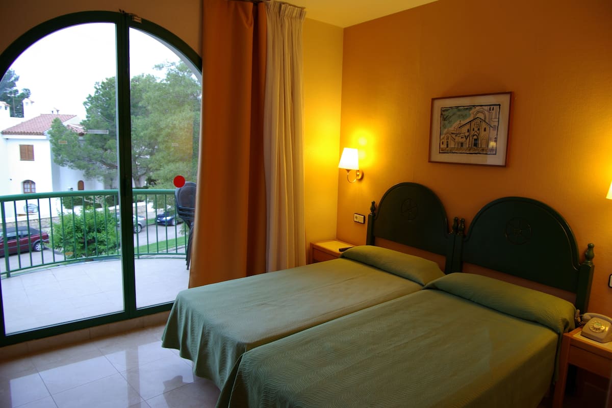Quarto de hotel com duas camas, varanda, vista para a rua e um quadro na parede.