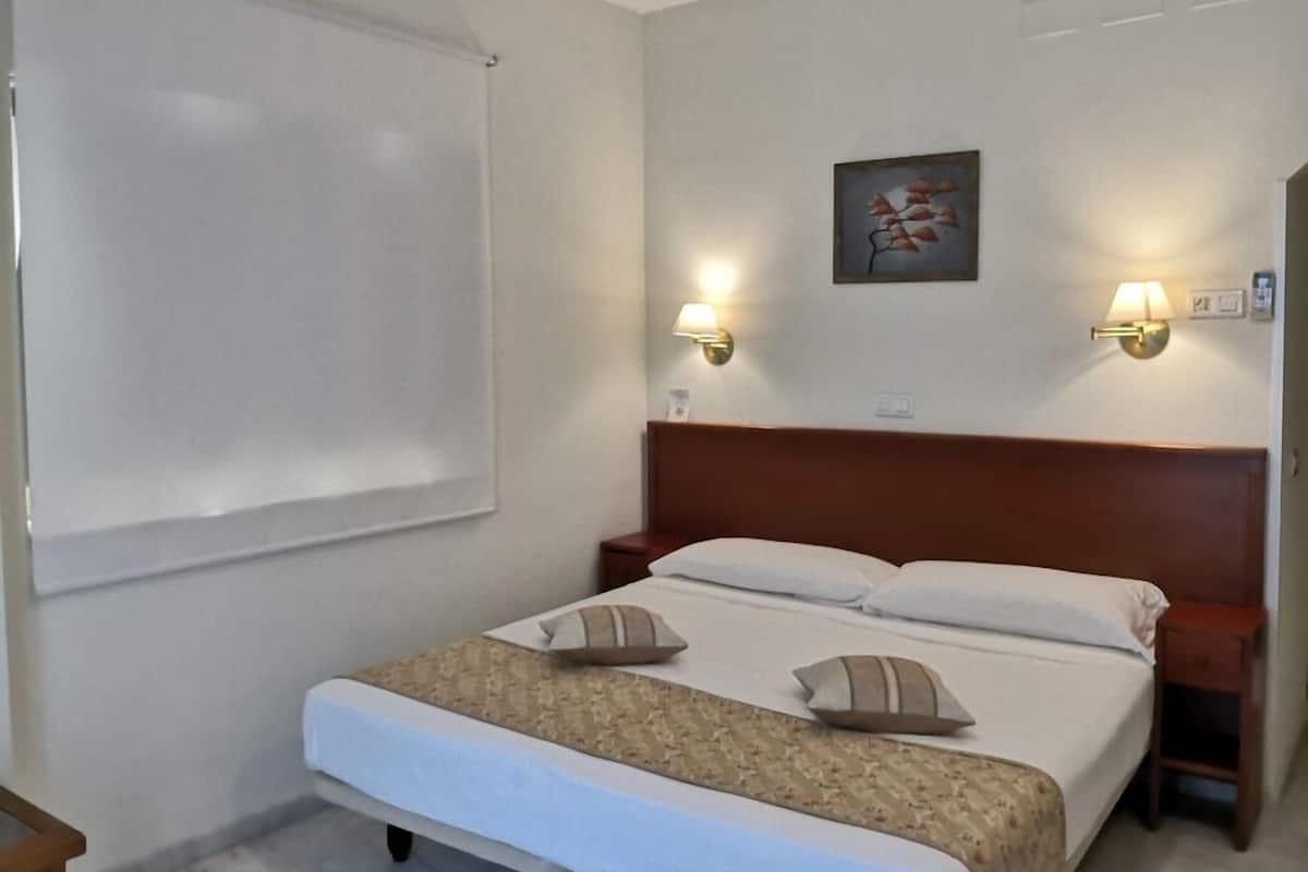 Quarto de hotel com uma cama, duas mesas de cabeceira, uma luminária na parede e um quadro.