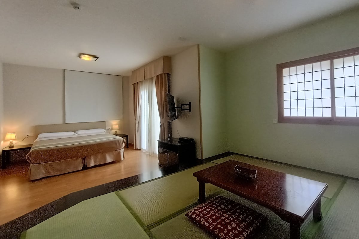 Quarto de hotel com cama, mesa de cabeceira, televisão e janela com vista.