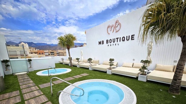 Uma área de piscina no terraço com duas banheiras de hidromassagem, espreguiçadeiras e uma parede com o logotipo do MB Boutique Hotel.