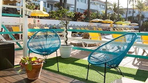 Uma área na piscina com espreguiçadeiras, uma mesa de madeira e um vaso de planta.