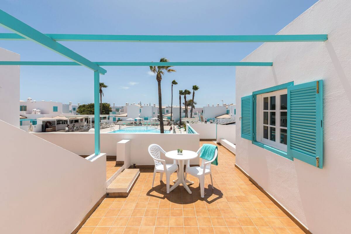 Terraço no telhado com piscina, cadeiras brancas e uma mesa.