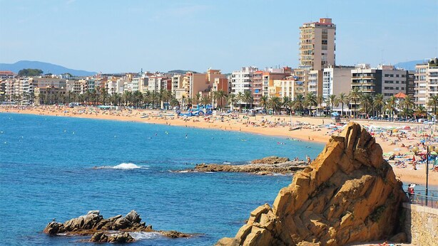 Paisagem costeira com praia, formações rochosas e edifícios altos.