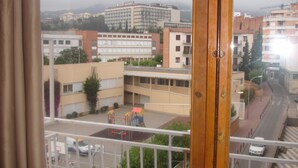 Vista da janela sobre uma paisagem urbana com edifícios, um parquinho e uma rua com um carro.