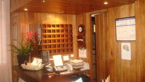 Um balcão de recepção de madeira com um computador, telefone e diversos documentos.