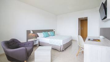 Quarto de hotel moderno com cama, uma cadeira, escrivaninha e televisão.
