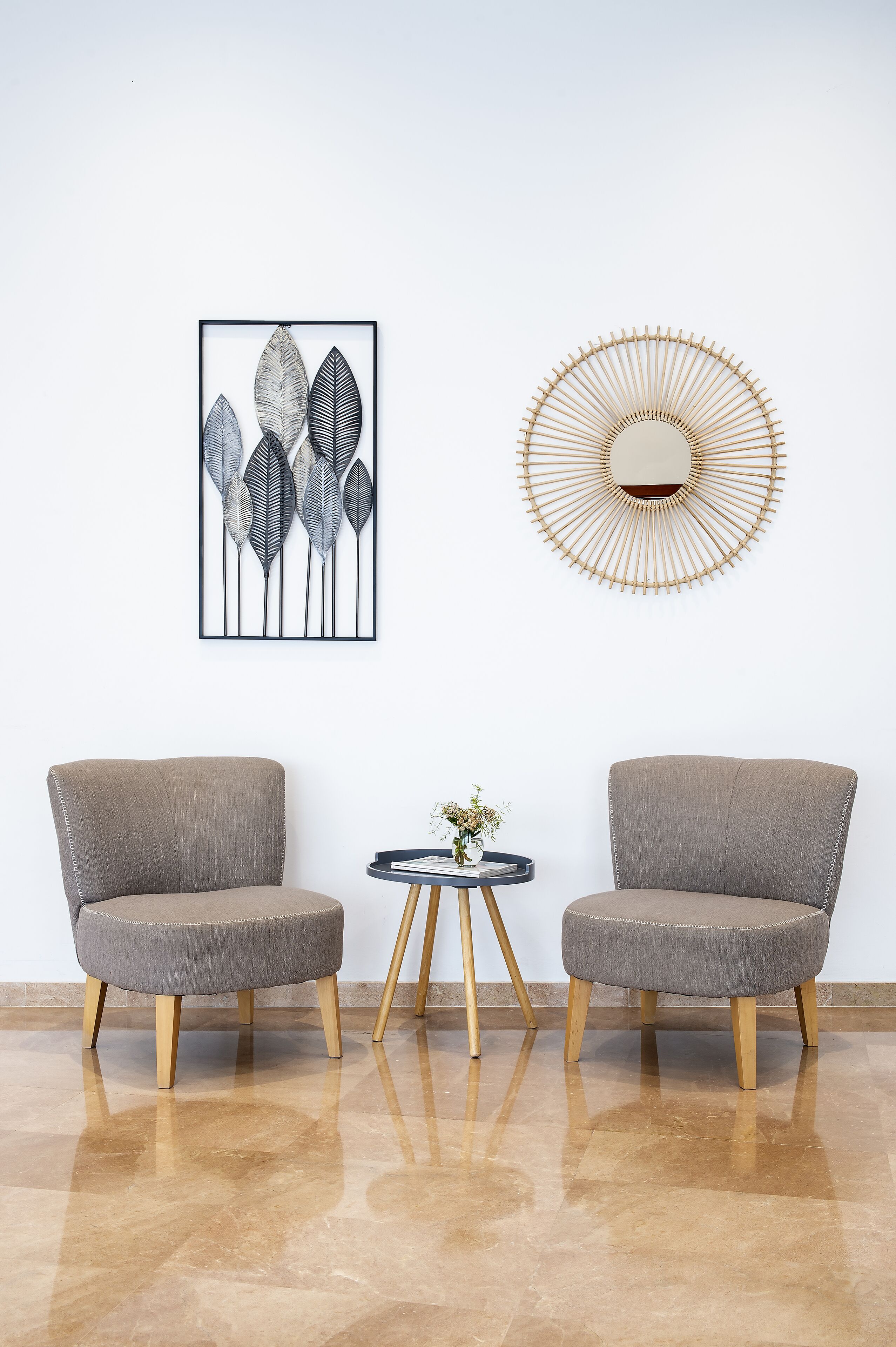 Um quarto com duas poltronas cinzentas, uma mesinha redonda com um vaso e duas obras de arte nas paredes.