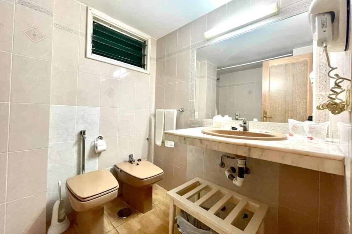 Casa de banho com sanita, lavatório, espelho e chuveiro.