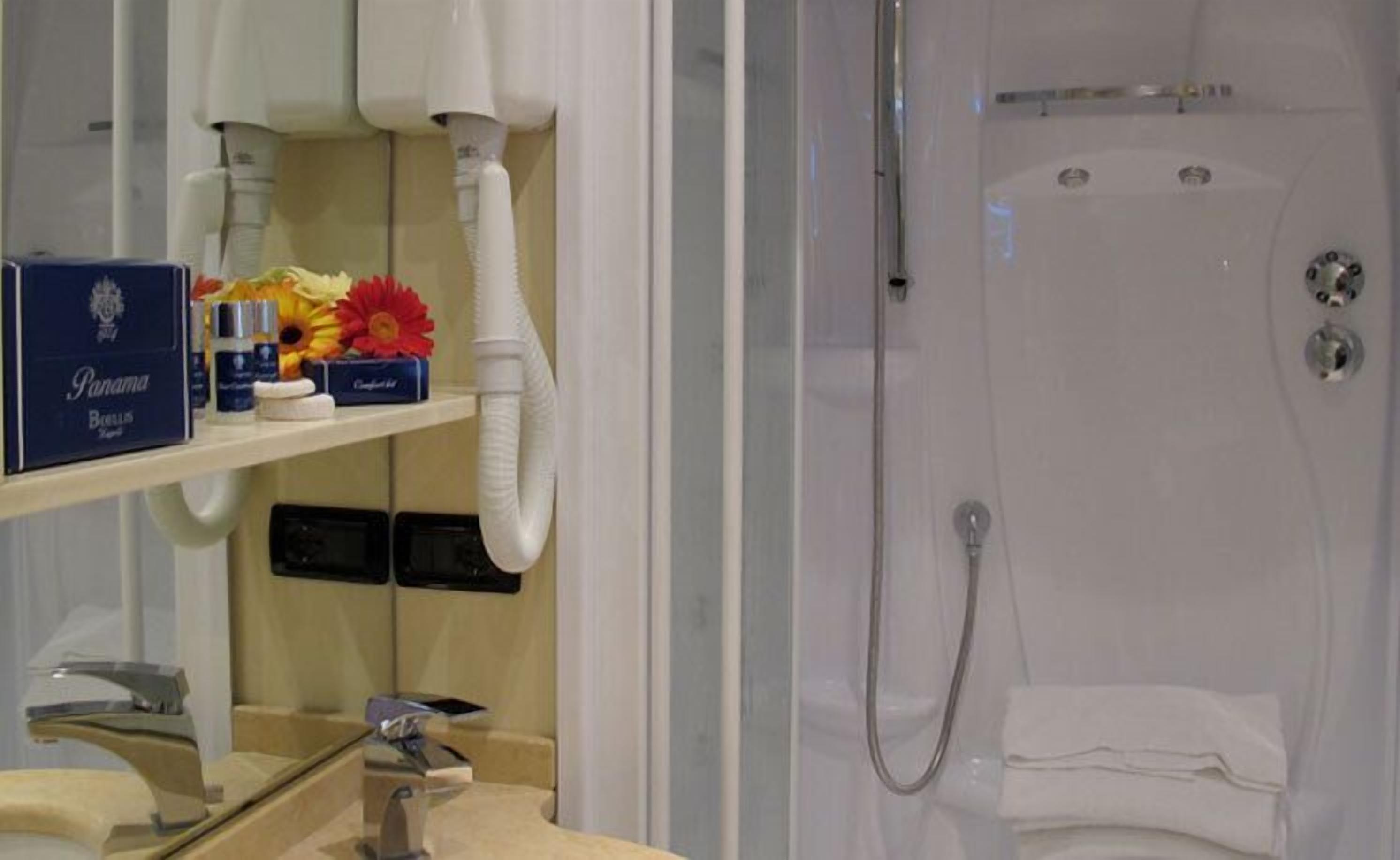 Uma casa de banho com chuveiro, lavatório e prateleira com artigos de higiene pessoal.