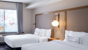 Quarto de hotel com duas camas, uma janela grande com cortinas, luminária fixada na parede e cabeceira de madeira.
