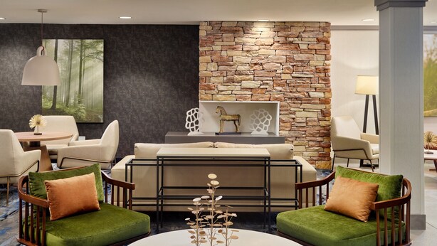 Um lobby moderno com parede decorada em pedra, uma mesa de centro redonda e cadeiras estofadas em verde.