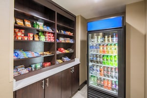 Uma área de autoatendimento com máquinas de venda de lanches e bebidas, incluindo diversas opções de salgadinhos embalados e bebidas em garrafa.