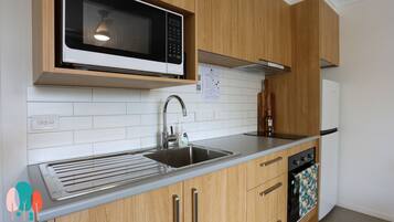 Uma cozinha moderna com armários de madeira, pia de aço inoxidável, micro-ondas e forno embutido.