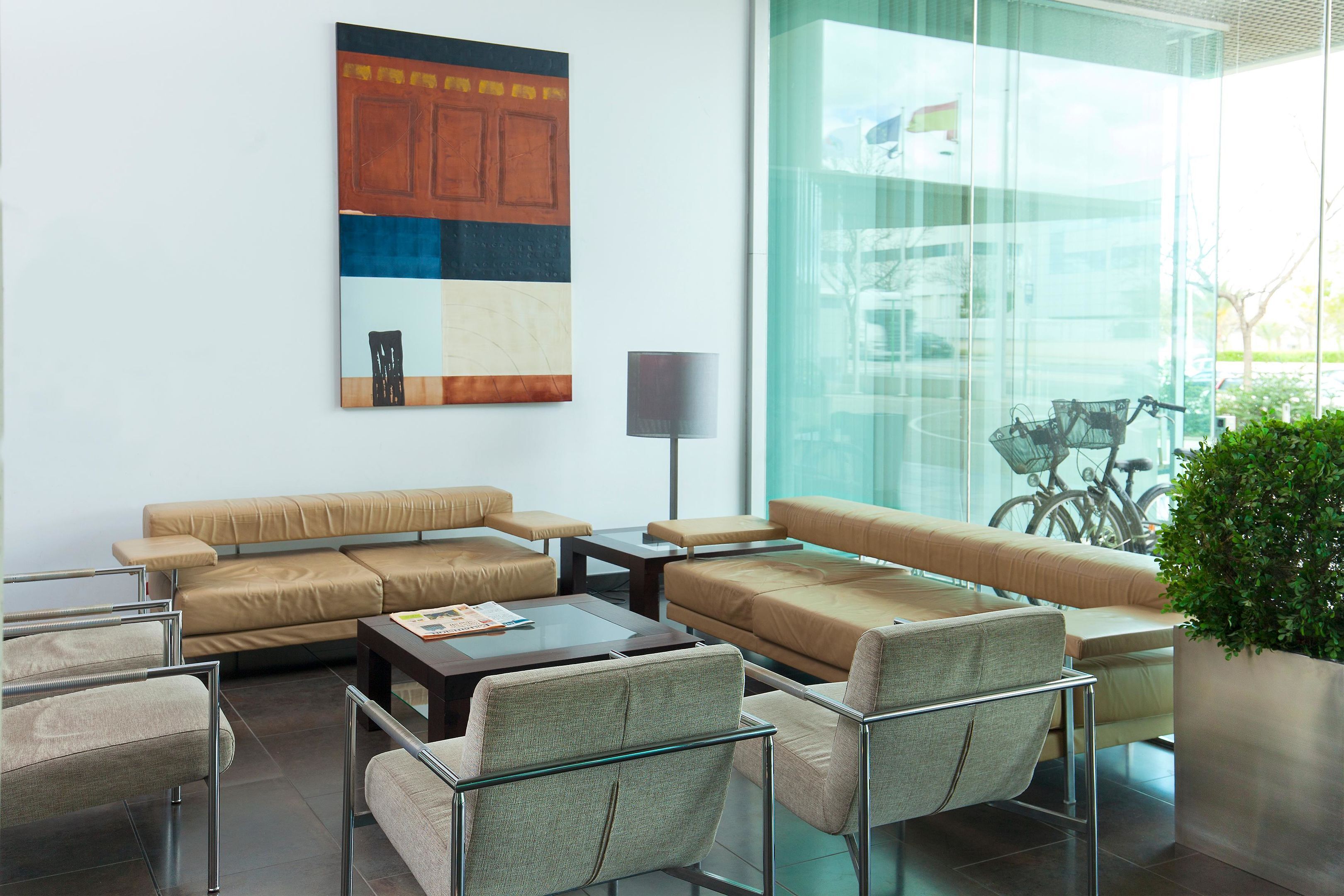 Uma área de espera moderna com sofás de couro, cadeiras com estrutura metálica, uma mesa de centro e uma grande pintura abstrata na parede.